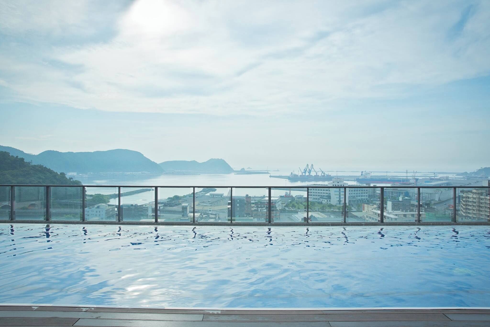 Piscina no terraço com vista para um porto e montanhas ao longe.