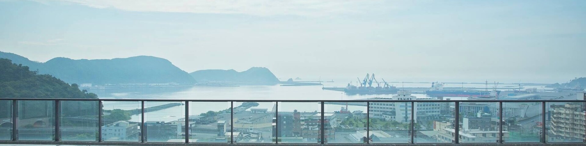 Piscina no terraço com vista para um porto e montanhas ao longe.