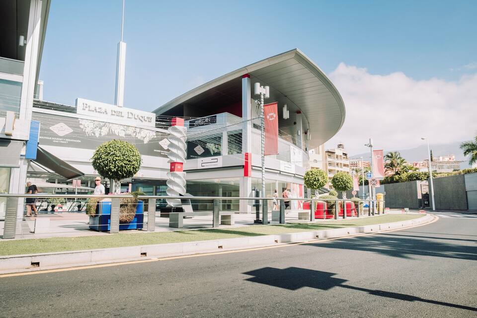 Um edifício moderno com telhado curvo e letreiro com a inscrição 'Plaza del Duque'.
