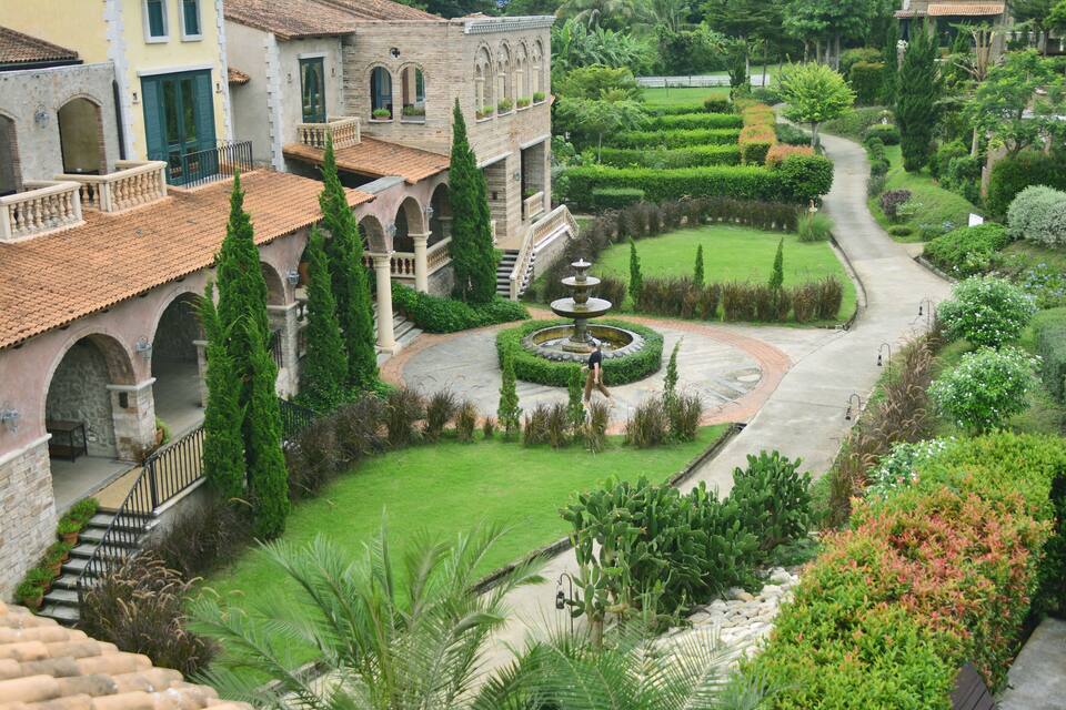 Um jardim exuberante com um caminho sinuoso, uma fonte e arquitetura clássica.