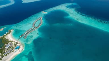 Vista aérea de um resort costeiro com um longo píer, águas turquesa cristalinas e uma praia de areia.