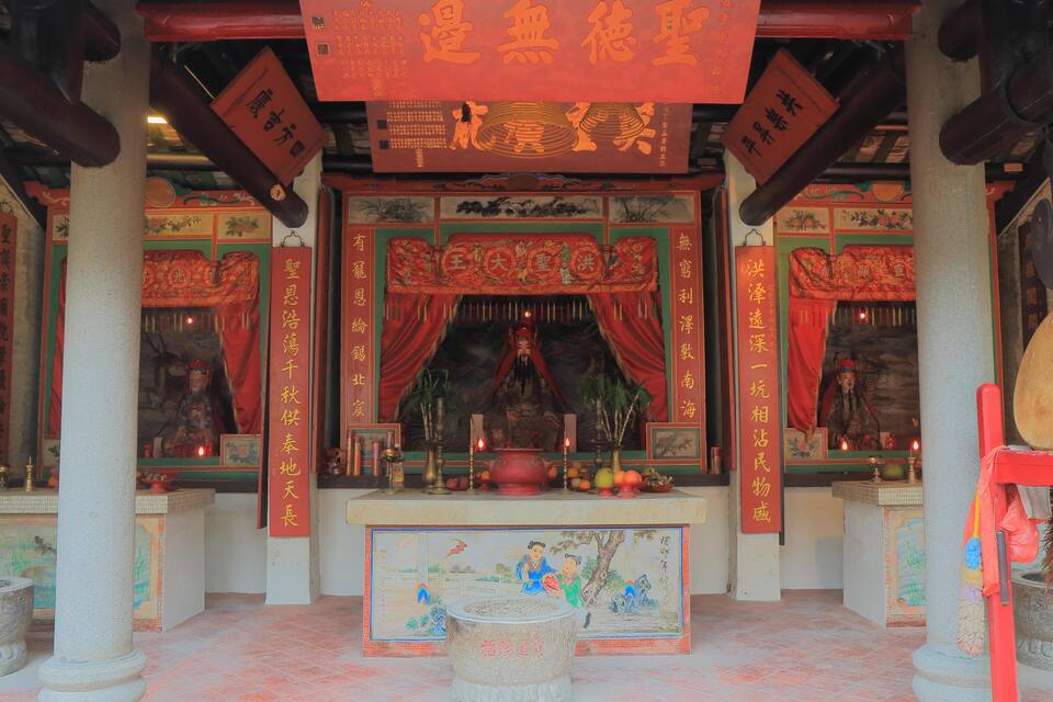Interior de um templo tradicional chinês, com decorações vermelhas, queimadores de incenso e um mural.