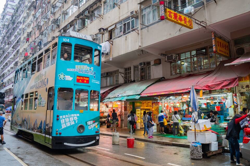 Um ônibus de dois andares azul em uma rua da cidade, com lojas e edifícios.