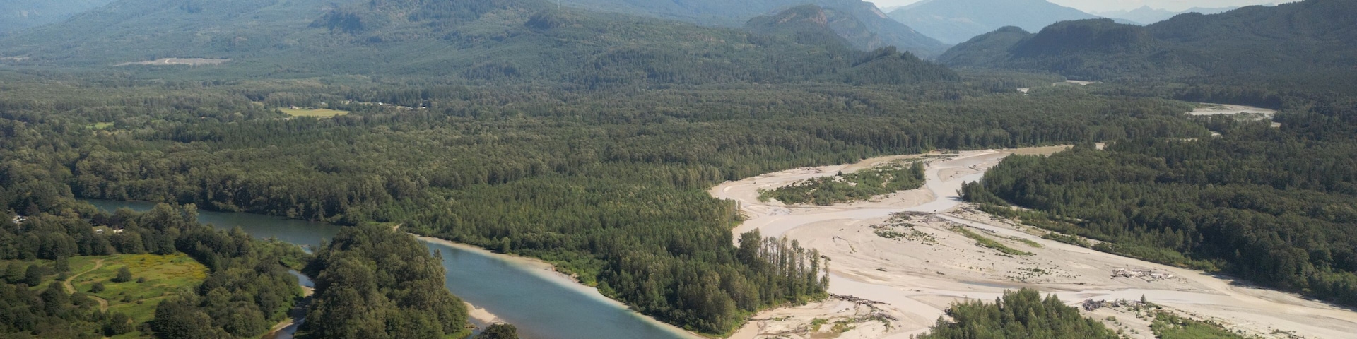 Um rio serpenteando por um vale arborizado, com montanhas ao fundo.