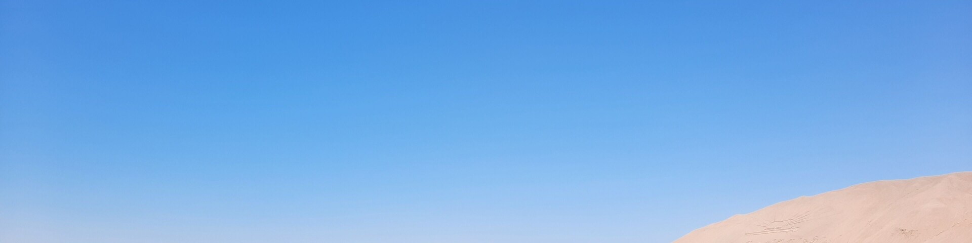 Mar azul e límpido com uma praia de areia e uma cadeia montanhosa ao longe.