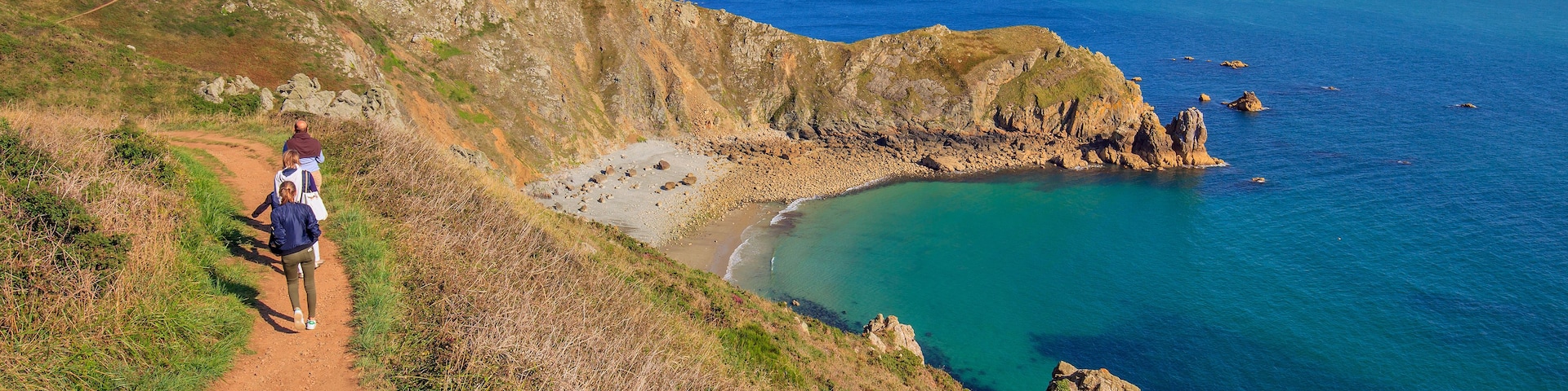 Trilha costeira com falésias rochosas e mar azul cristalino.