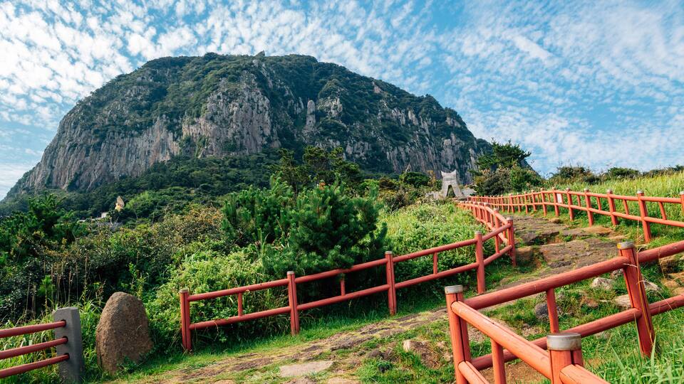 Paisagem montanhosa com uma cerca de metal vermelha que leva a um afloramento rochoso.
