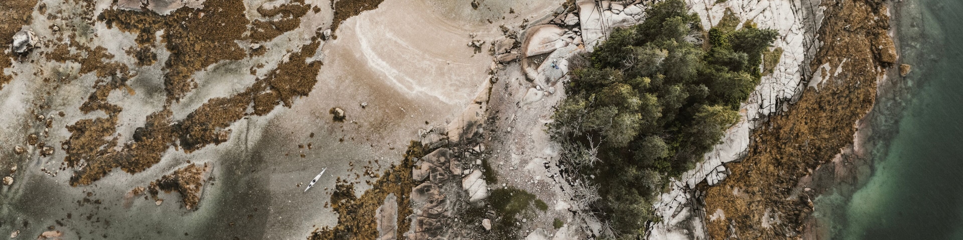 Paisagem costeira com costas rochosas, águas cristalinas e vegetação escassa.