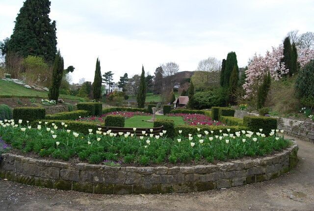 Um jardim formal com sebes bem aparadas, diversas plantas floridas e um caminho de pedra.