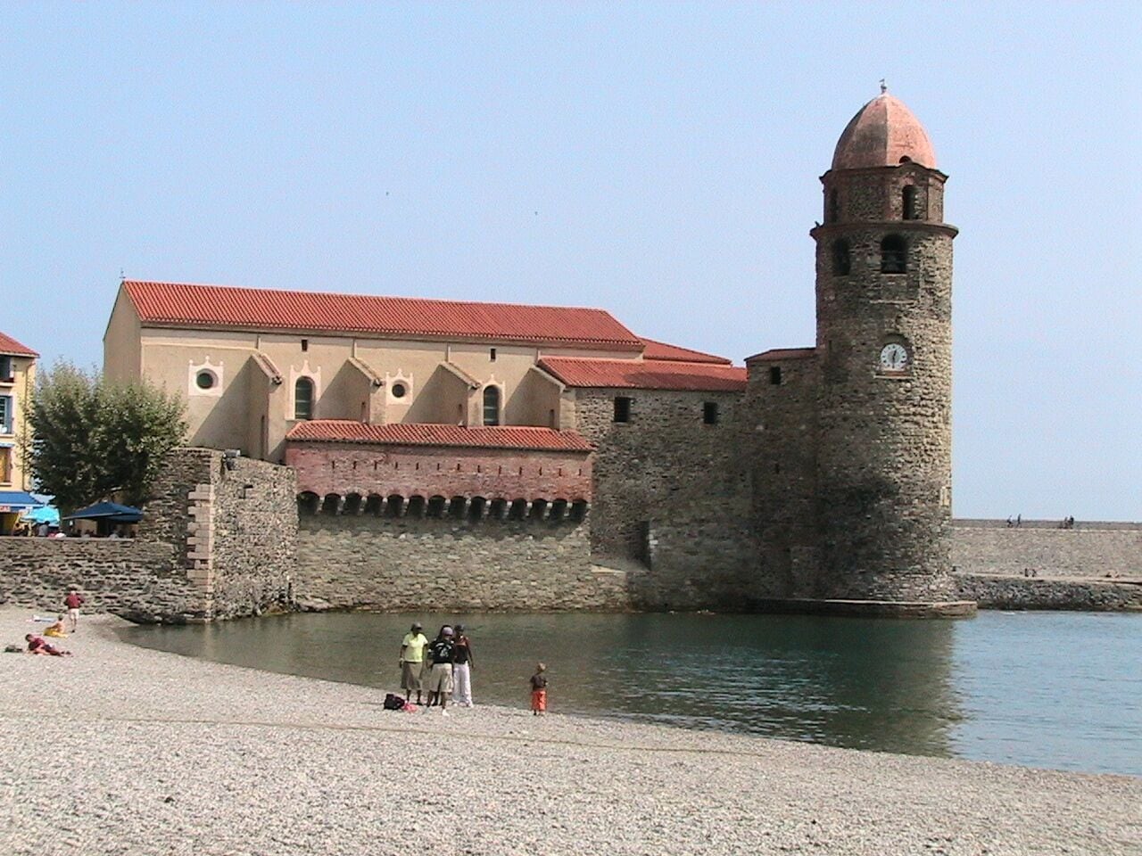 Um edifício histórico com telhado de telhas vermelhas e uma torre de pedra, à beira de águas calmas.