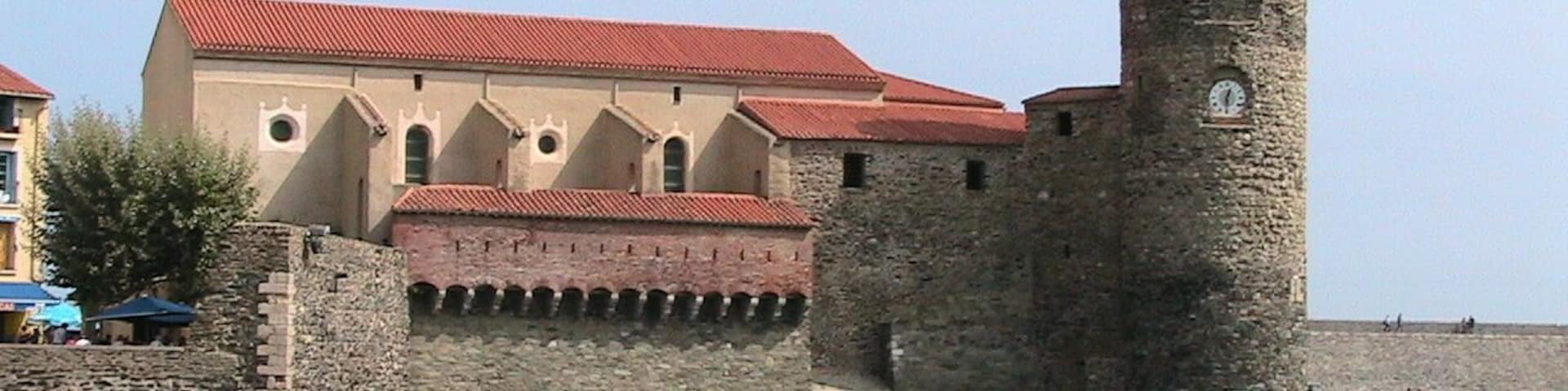 Um edifício histórico com telhado de telhas vermelhas e uma torre de pedra, à beira de águas calmas.