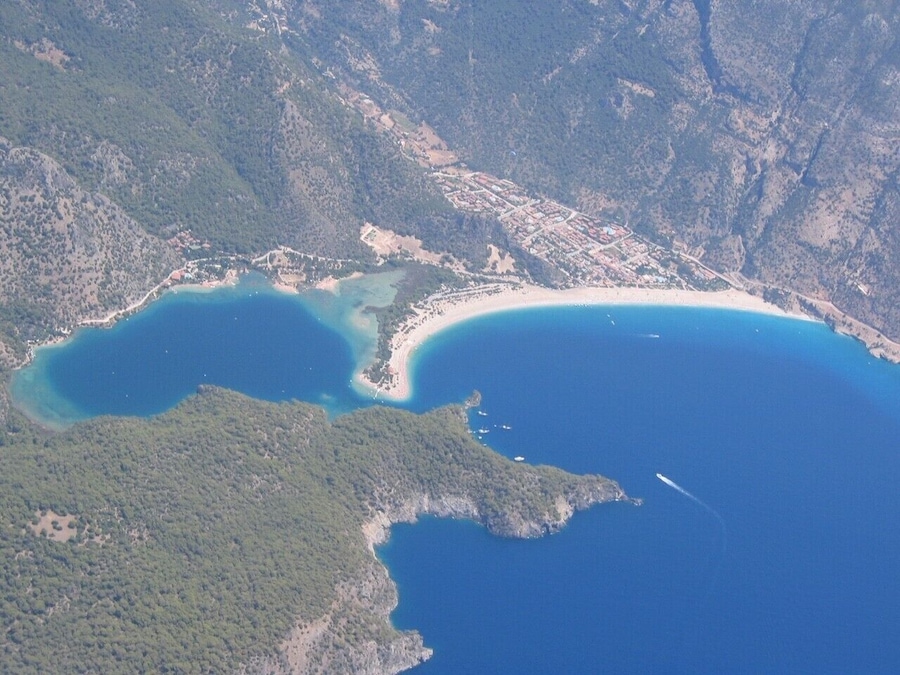 Vista aérea de uma área costeira com uma grande baía, uma pequena ilha e montanhas ao redor.
