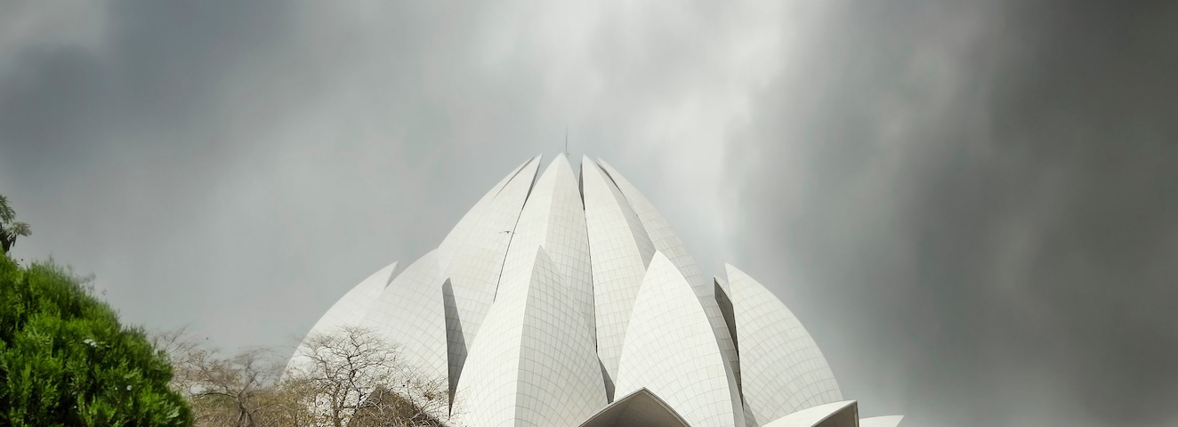 Um edifício branco imponente com design arquitetônico singular, cercado por vegetação sob um céu nublado.