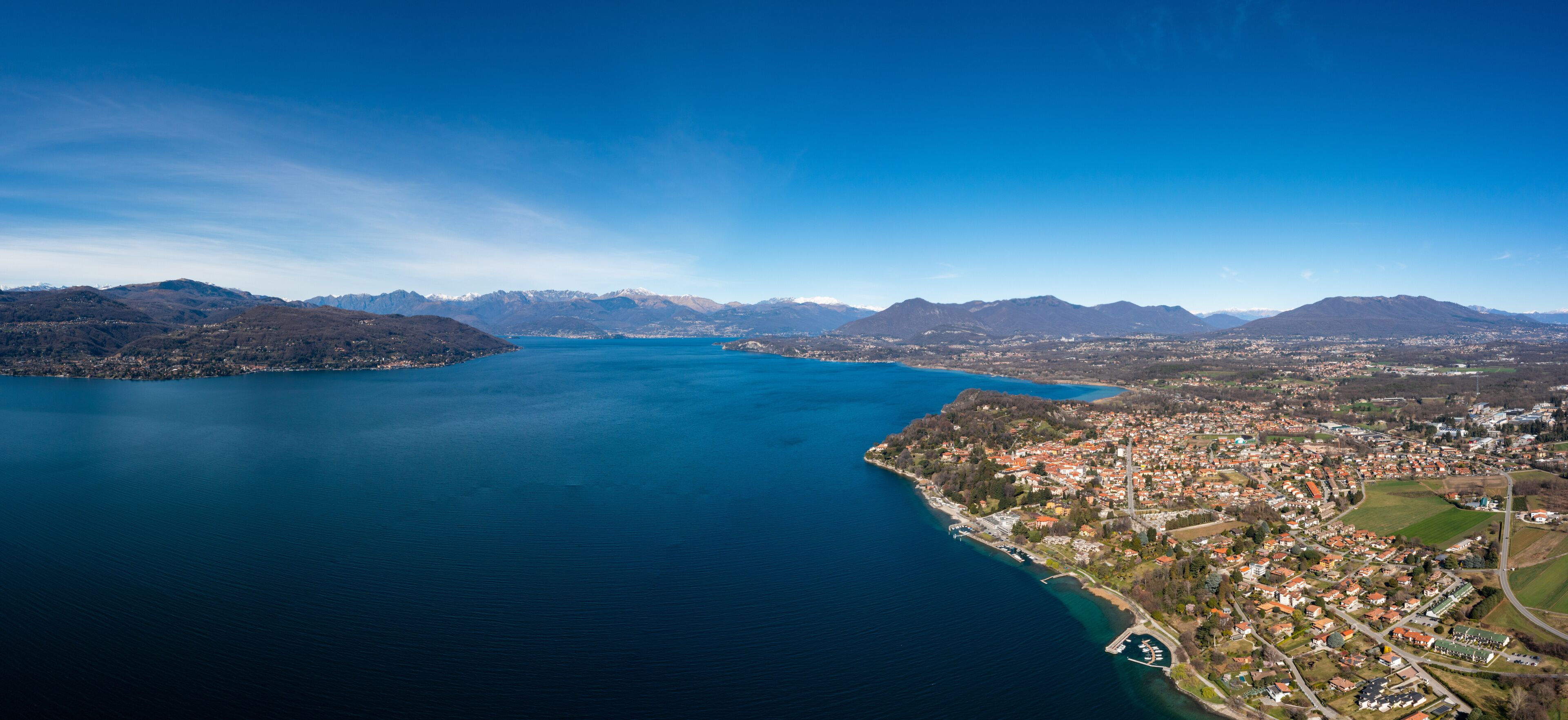 Vista panorâmica de uma cidade costeira, com uma grande extensão de água, montanhas ao fundo e céu claro.