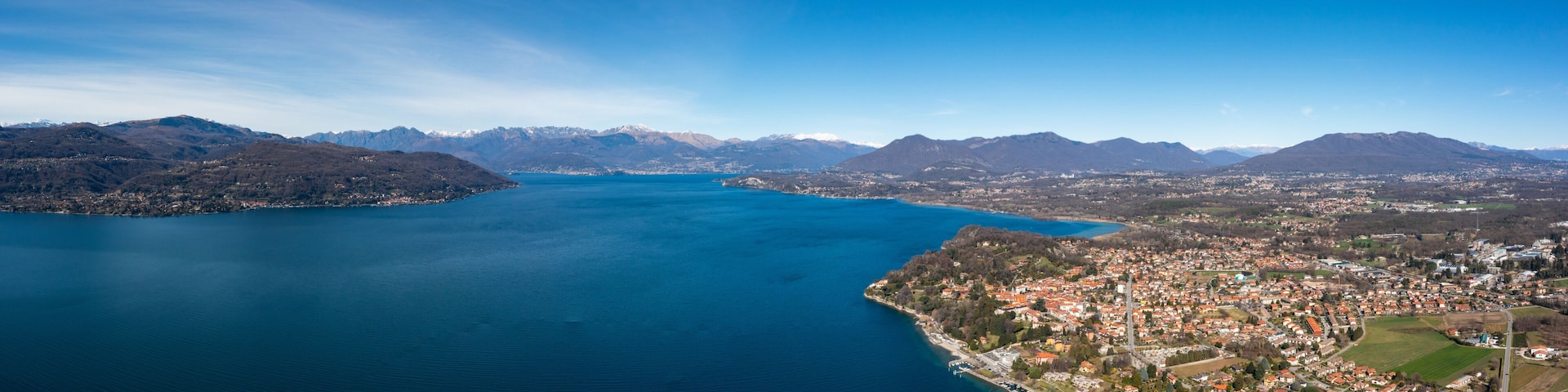 Vista panorâmica de uma cidade costeira, com uma grande extensão de água, montanhas ao fundo e céu claro.