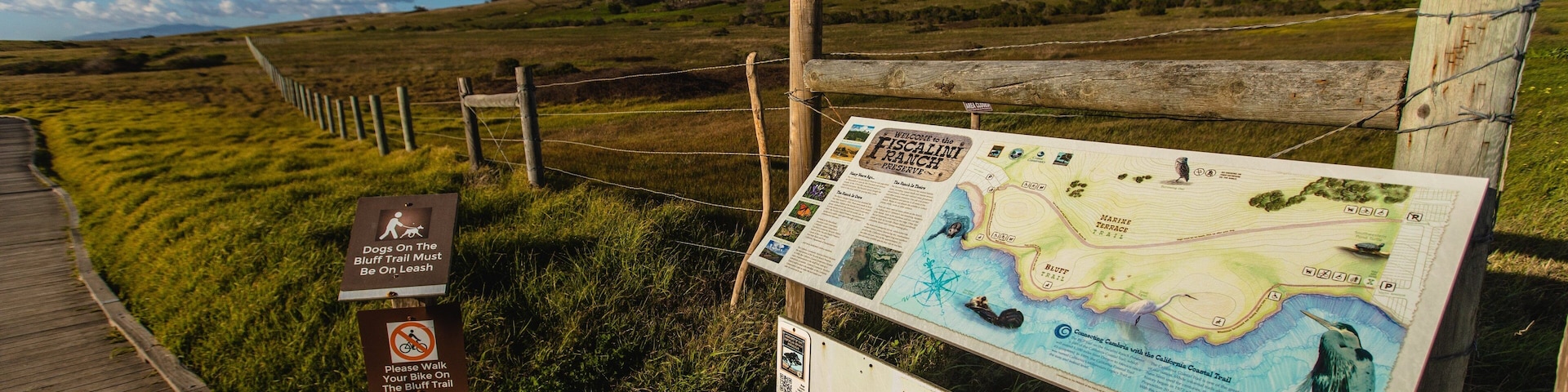 Uma passarela de madeira leva a um grande painel informativo sobre a Trilha do Bluff.