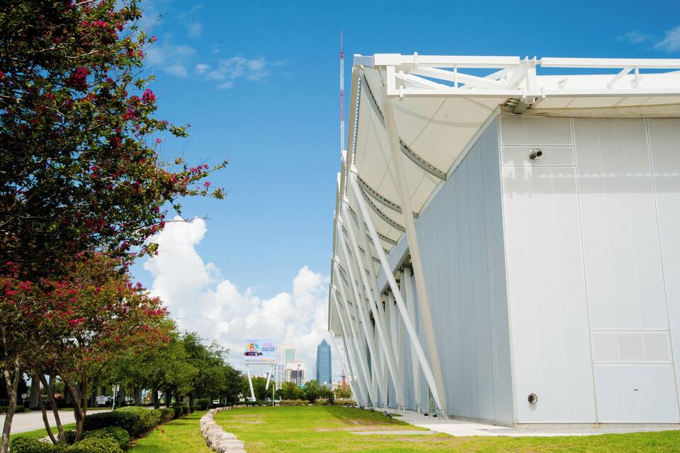 Um edifício moderno com fachada branca e design arquitetônico singular, cercado por vegetação exuberante e céu azul límpido.