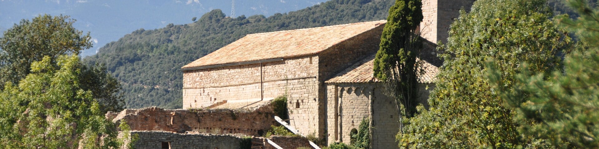 Um edifício de pedra com telhado de cerâmica, rodeado por árvores e montanhas ao fundo.