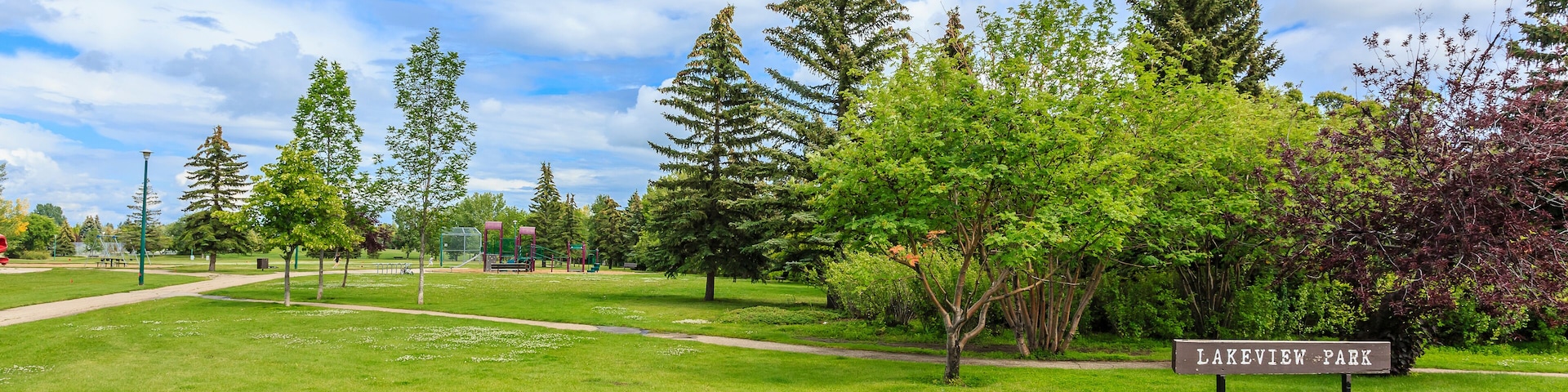 Um parque com uma placa indicando 'LAKEVIEW PARK', grama verde, árvores e um parquinho.