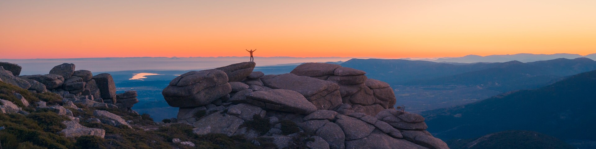 Uma pessoa em uma formação rochosa com o pôr do sol ao fundo.