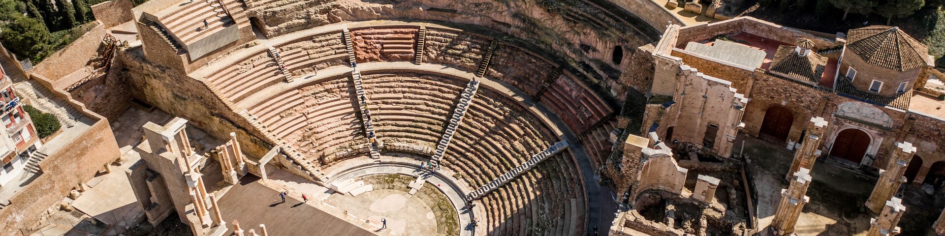 Um anfiteatro antigo rodeado por edifícios modernos e árvores.