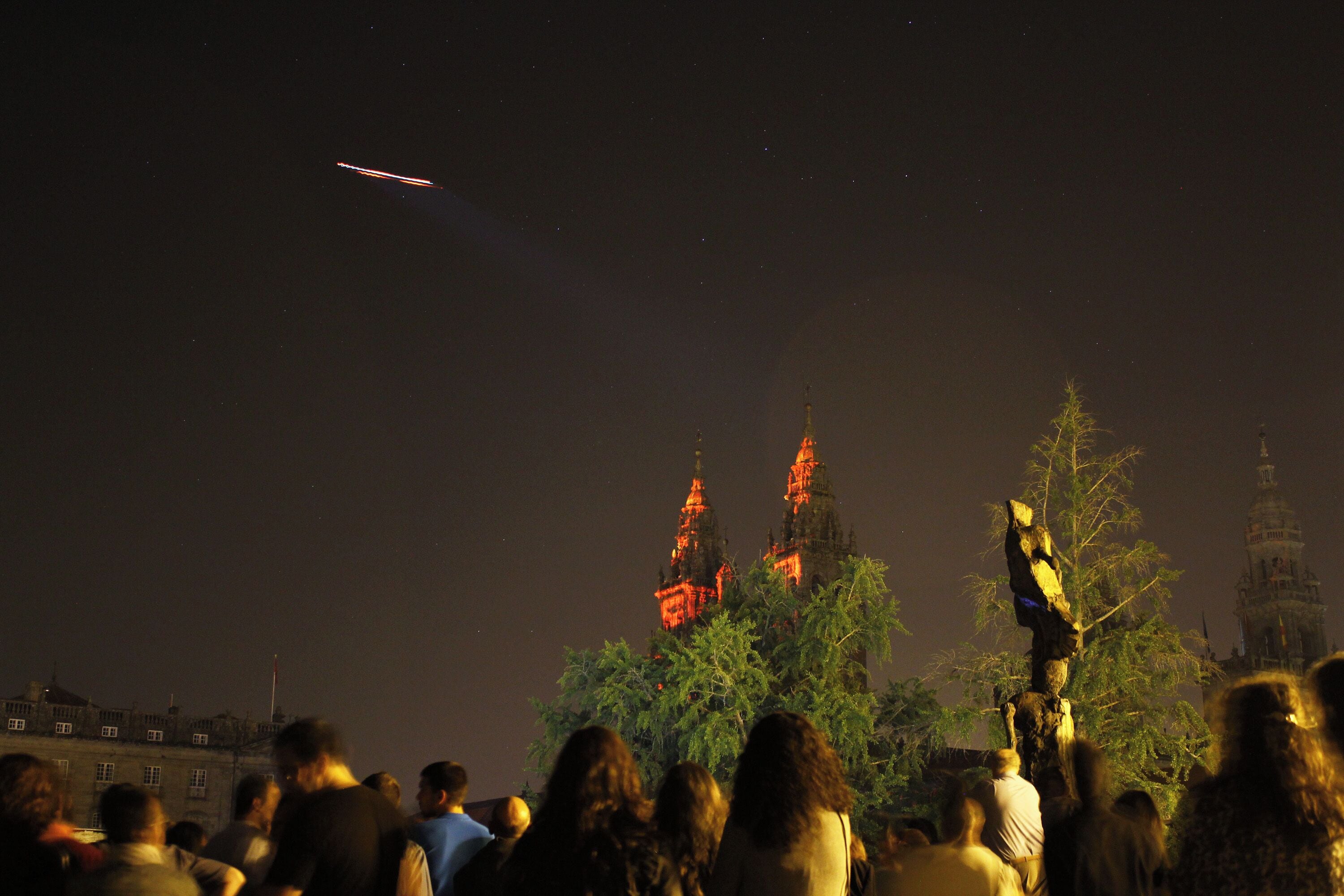 Cena noturna com uma multidão de pessoas, um templo bem iluminado e uma torre ao fundo.