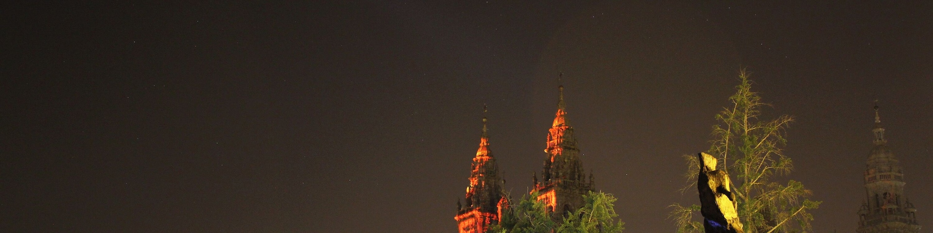 Cena noturna com uma multidão de pessoas, um templo bem iluminado e uma torre ao fundo.