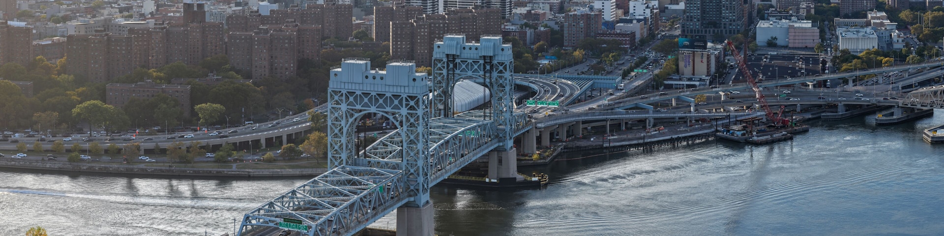 Uma grande ponte de aço atravessa um rio, cercada por uma densa paisagem urbana com arranha-céus.