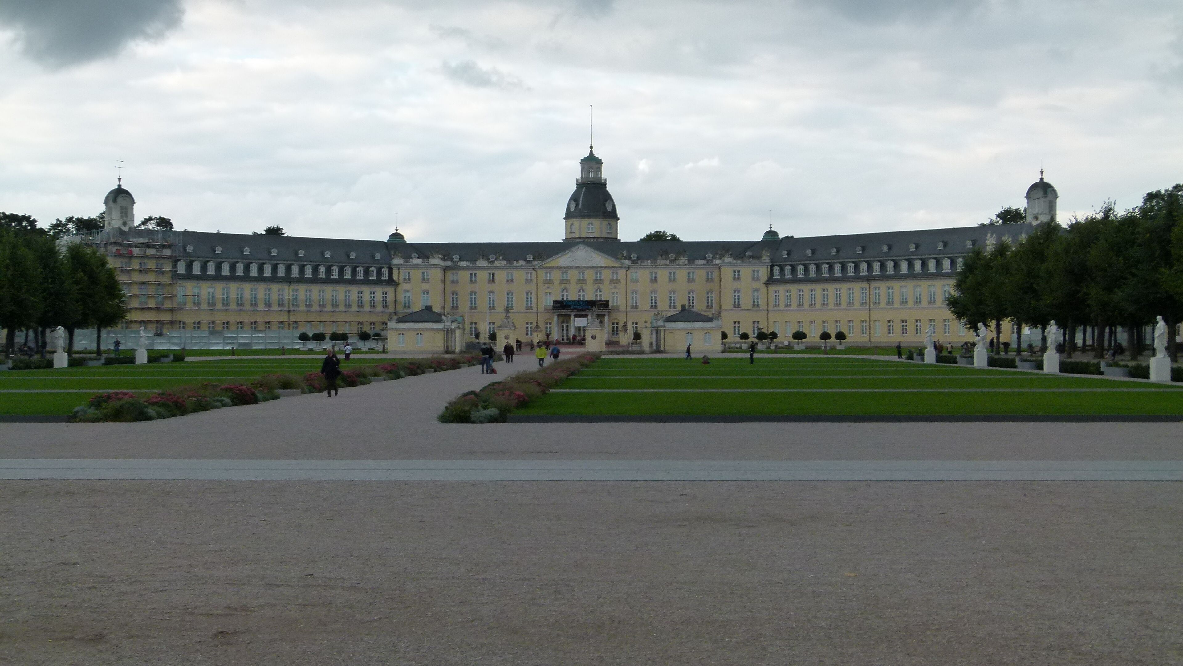 Um edifício histórico imponente, com arquitetura simétrica, uma cúpula central e um jardim formal com estátuas.