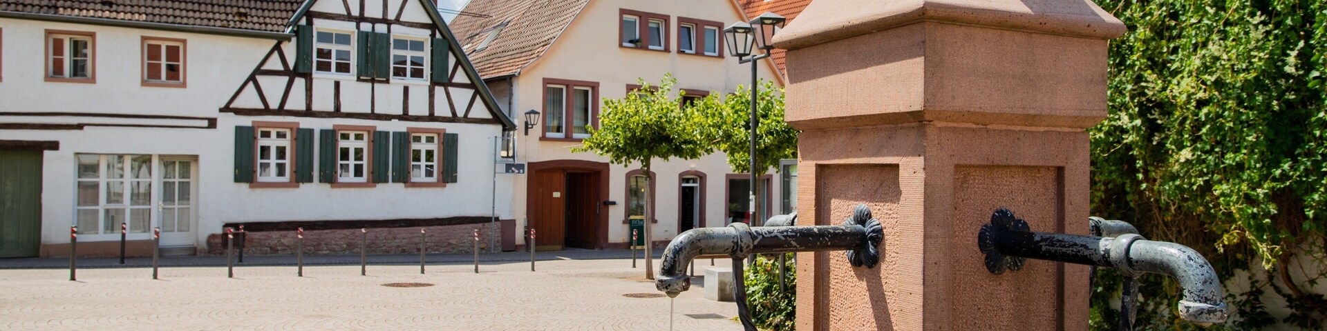Uma praça tradicional europeia com edifícios históricos, uma fonte de água e calçada de pedra.