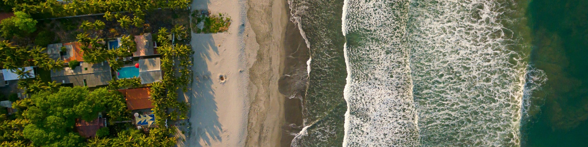 Uma praia com ondas, uma piscina e casas.