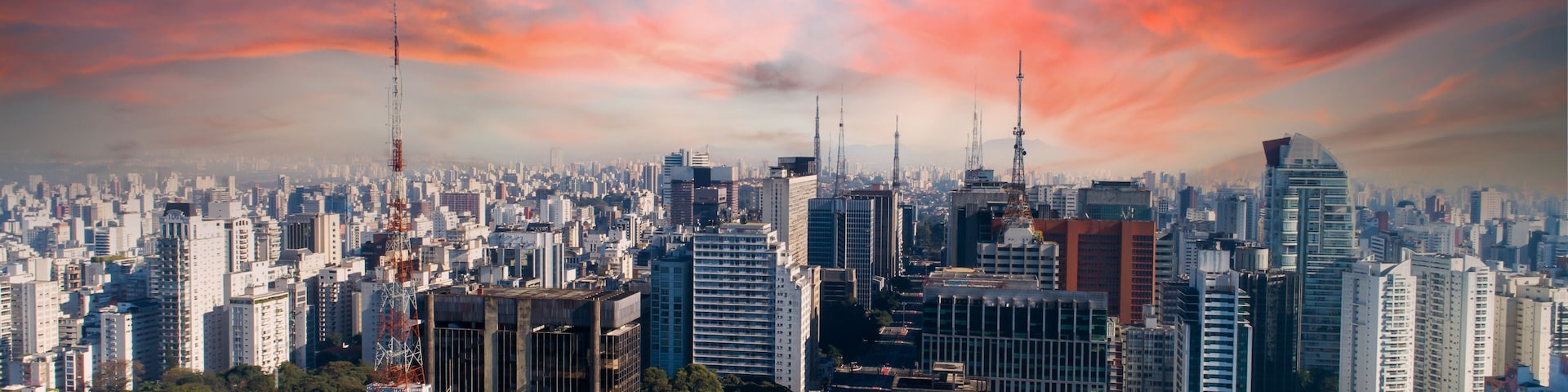 Uma paisagem urbana com um conjunto denso de edifícios altos, uma torre imponente e um céu de pôr do sol dramático.