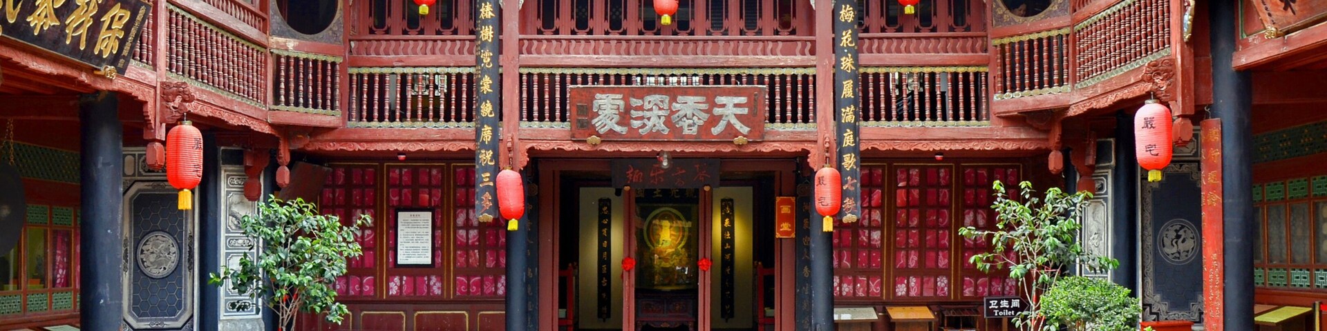 Um pátio tradicional chinês com lanternas vermelhas, telhados em azulejo e portas de madeira ricamente decoradas.
