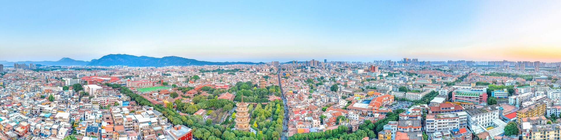 Vista panorâmica de uma cidade com intenso desenvolvimento urbano, um rio notável e montanhas ao longe.