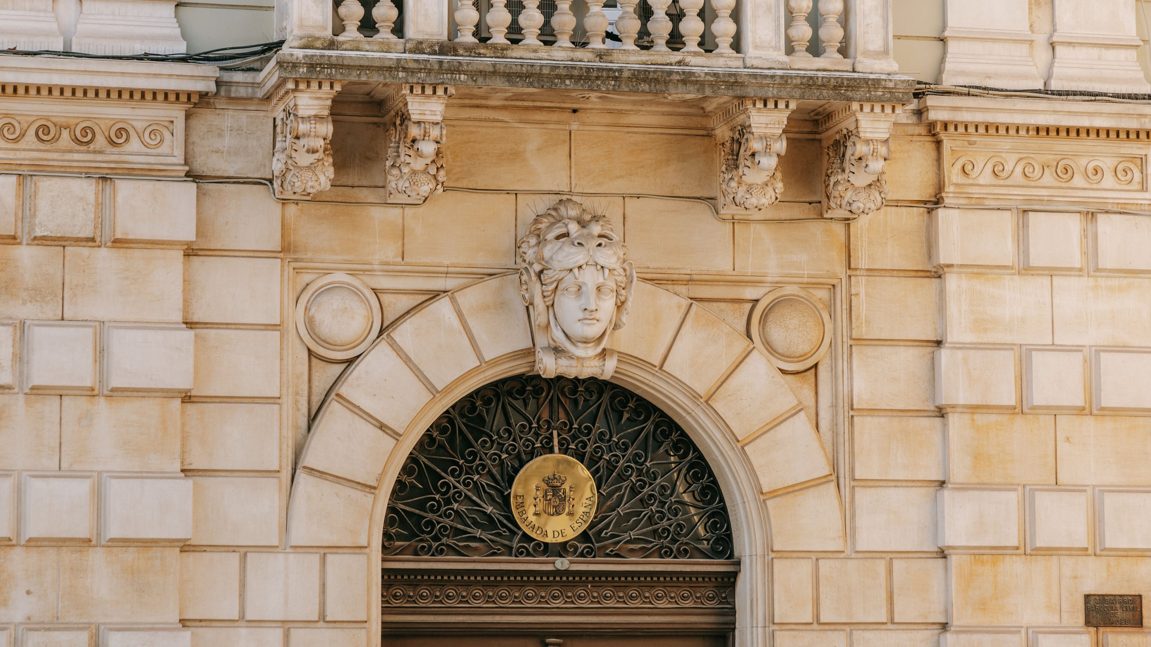 Fachada de pedra detalhada com um arco decorativo, trabalhos em metal ornamentais e um emblema de brasão.
