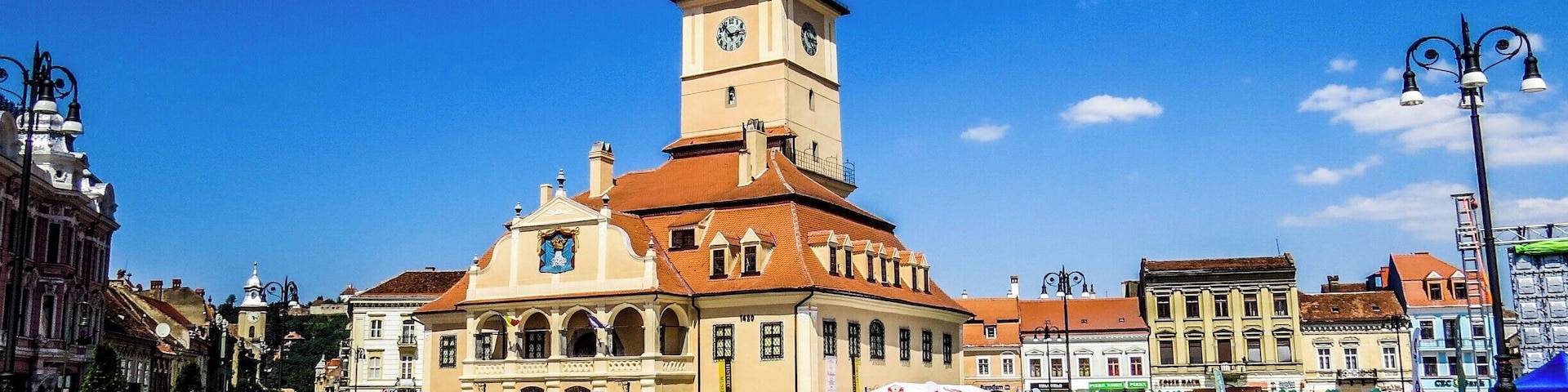 Uma praça histórica com uma torre do relógio imponente, uma grande área aberta e edifícios ao redor.