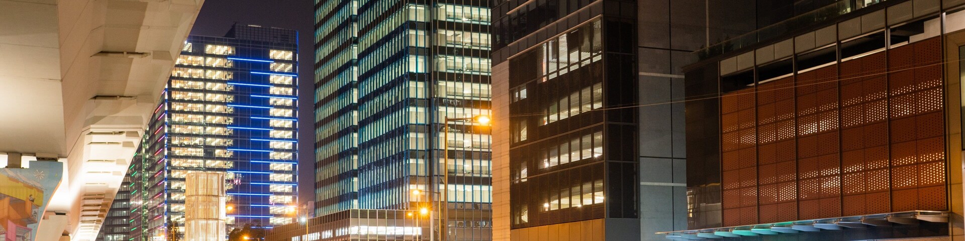 Paisagem urbana noturna com edifícios modernos e janelas iluminadas.