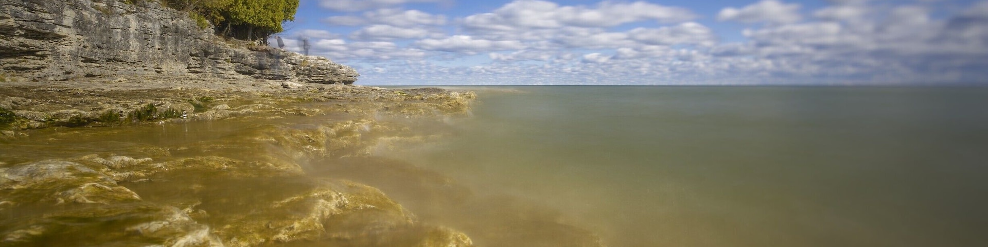 In Door county there is this small county park. It is very unassuming form the drive in. On its coast though lies stunning rock formations. The lake has eaten away at the soft rock and lowered the shelf so water is only a few inches deep.
I put on my super ND filter and just placed the camera on a small rock just above the water to take this. This actually looks away form the small caves that the park is known for.