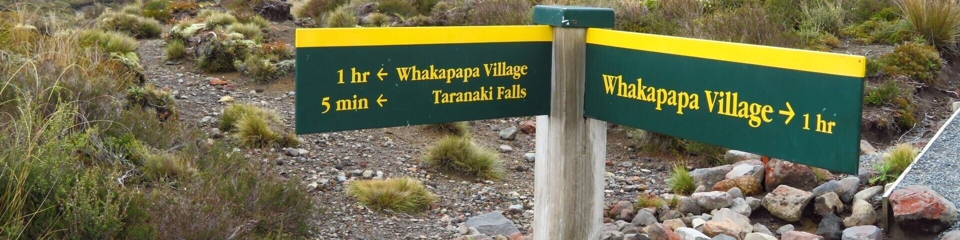 Placa de direção com indicações para Whakapapa Village e Taranaki Falls, mostrando os tempos de viagem.