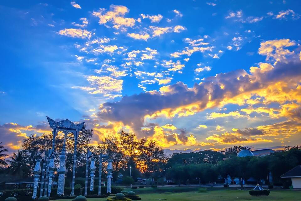 Céu com o sol poente e nuvens, um portão tradicional e um parque com árvores e relva.