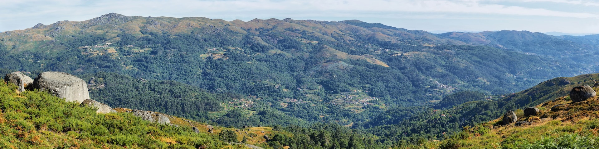 Paisagem montanhosa com florestas densas e afloramentos rochosos dispersos.