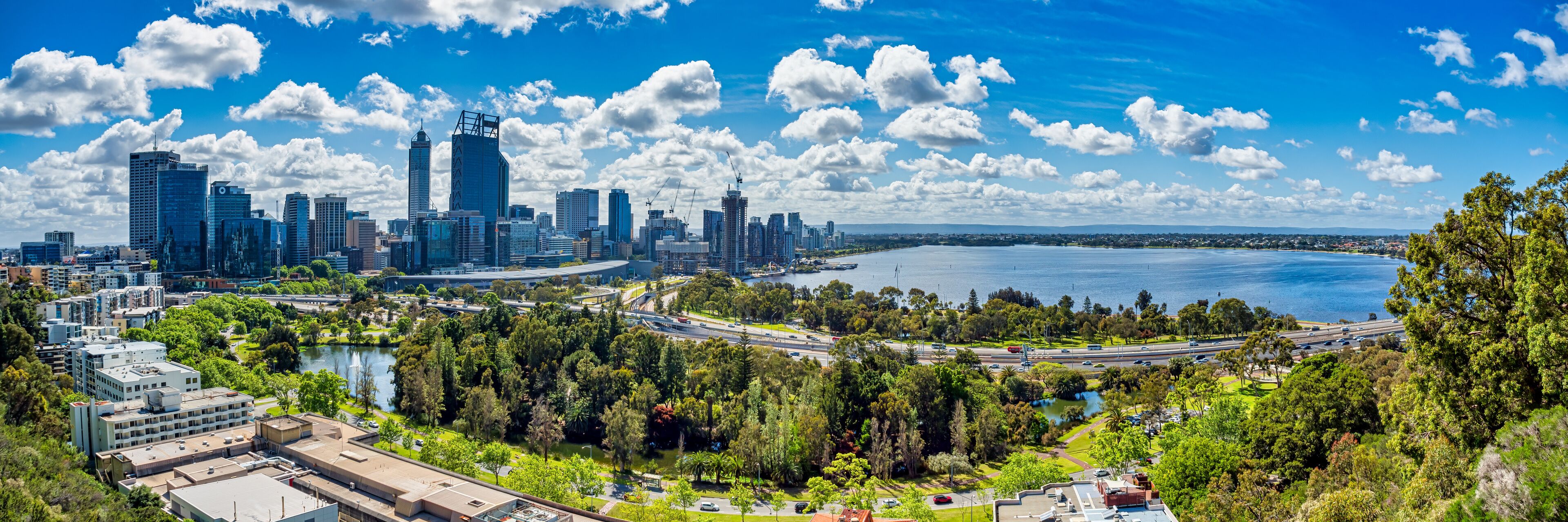 Silhueta urbana com arranha-céus modernos, uma extensa área de água e vegetação ao redor.