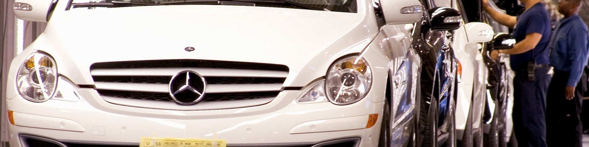 Um carro Mercedes-Benz branco em linha de montagem de fábrica, com trabalhadores.