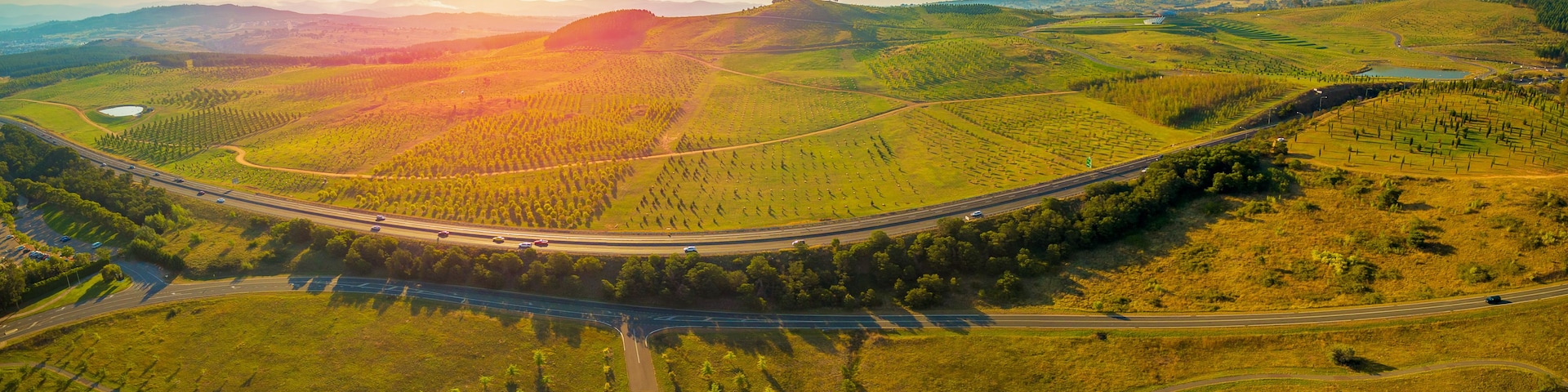 Uma estrada sinuosa serpenteando por uma paisagem ondulada, com campos e um pequeno lago.