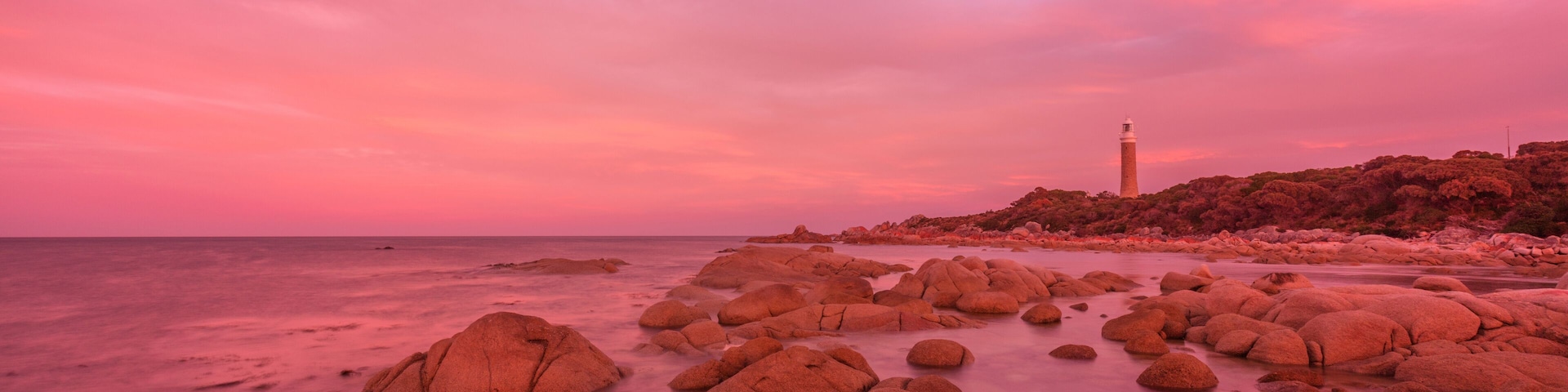 Uma costa rochosa com um farol ao longe durante o pôr do sol.