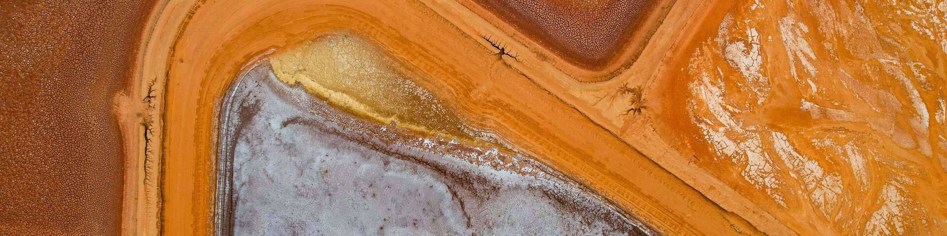 Vista aérea de uma paisagem com uma grande massa de água, uma área laranja bem definida e uma área branca com um pedaço amarelo.