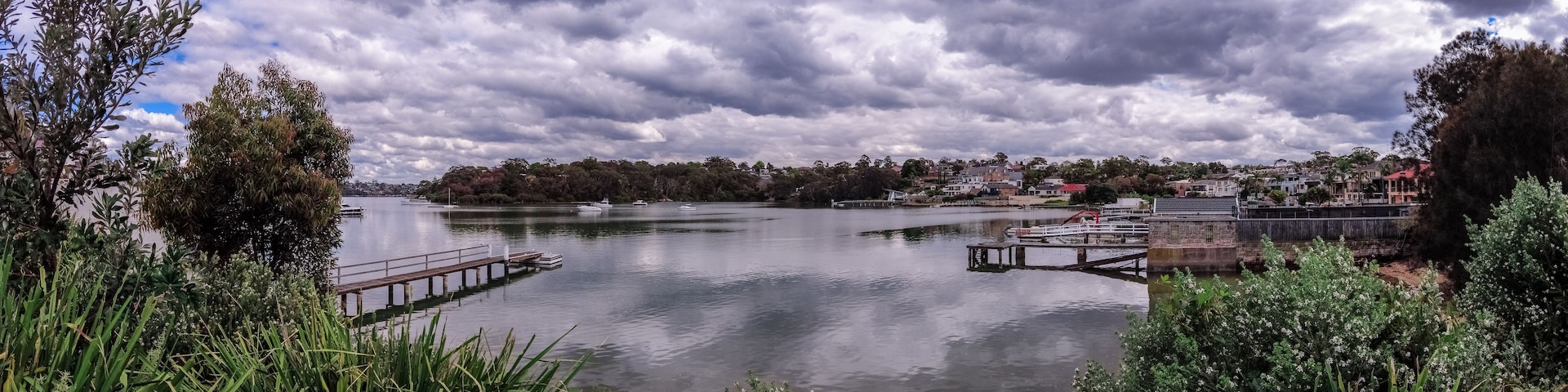 Um lago tranquilo com barcos, um cais e uma ponte que liga a uma cidade com edifícios.