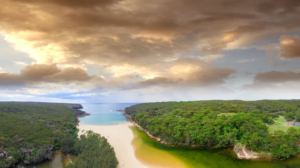 Paisagem costeira com rio, praia e colinas arborizadas.