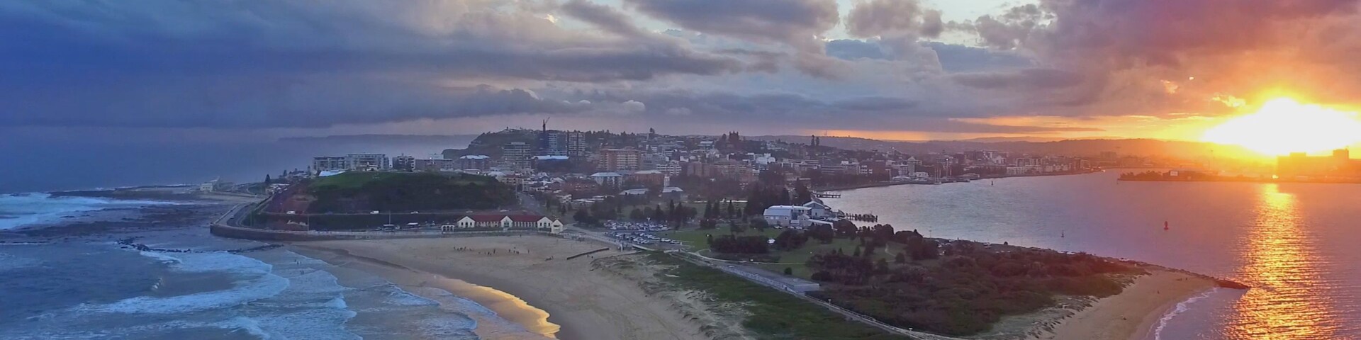 Paisagem costeira urbana com praia, ondas do oceano e pôr do sol.