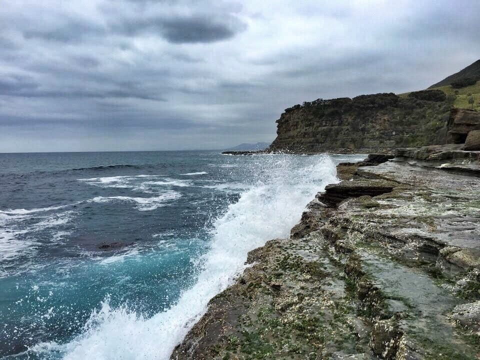 Litoral rochoso com ondas quebrando na costa sob um céu nublado.